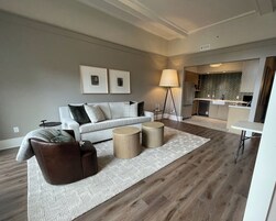 Sala de estar moderna com sofá, mesa de centro e uma pequena área de cozinha ao fundo.