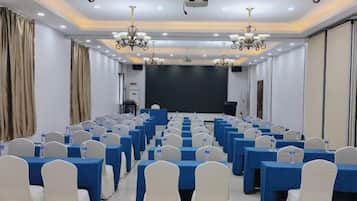Uma sala de conferências com fileiras de mesas e cadeiras, uma tela de projetor e um palco.