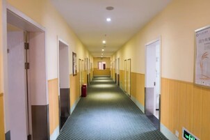 Corredor de hotel com portas em ambos os lados, carpete estampado e extintor de incêndio na parede.