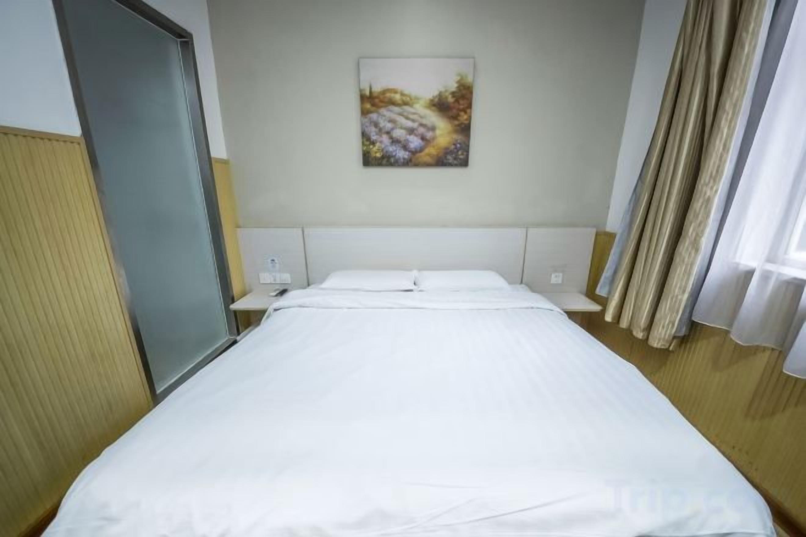 Quarto de hotel com cama, mesa de cabeceira, quadro na parede e cortinas na janela.