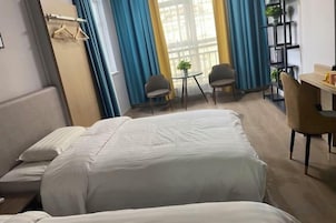 Quarto de hotel com duas camas, uma escrivaninha, cadeiras e uma pequena mesa com uma planta.