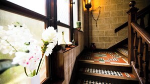 Uma escadaria com ladrilhos estampados, corrimão de madeira e um candeeiro fixado na parede.