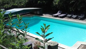 Piscina retangular com deck de madeira ao redor, com árvores proporcionando sombra.