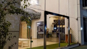 Um edifício moderno com entrada de vidro, interior branco e área gramada sintética na frente.