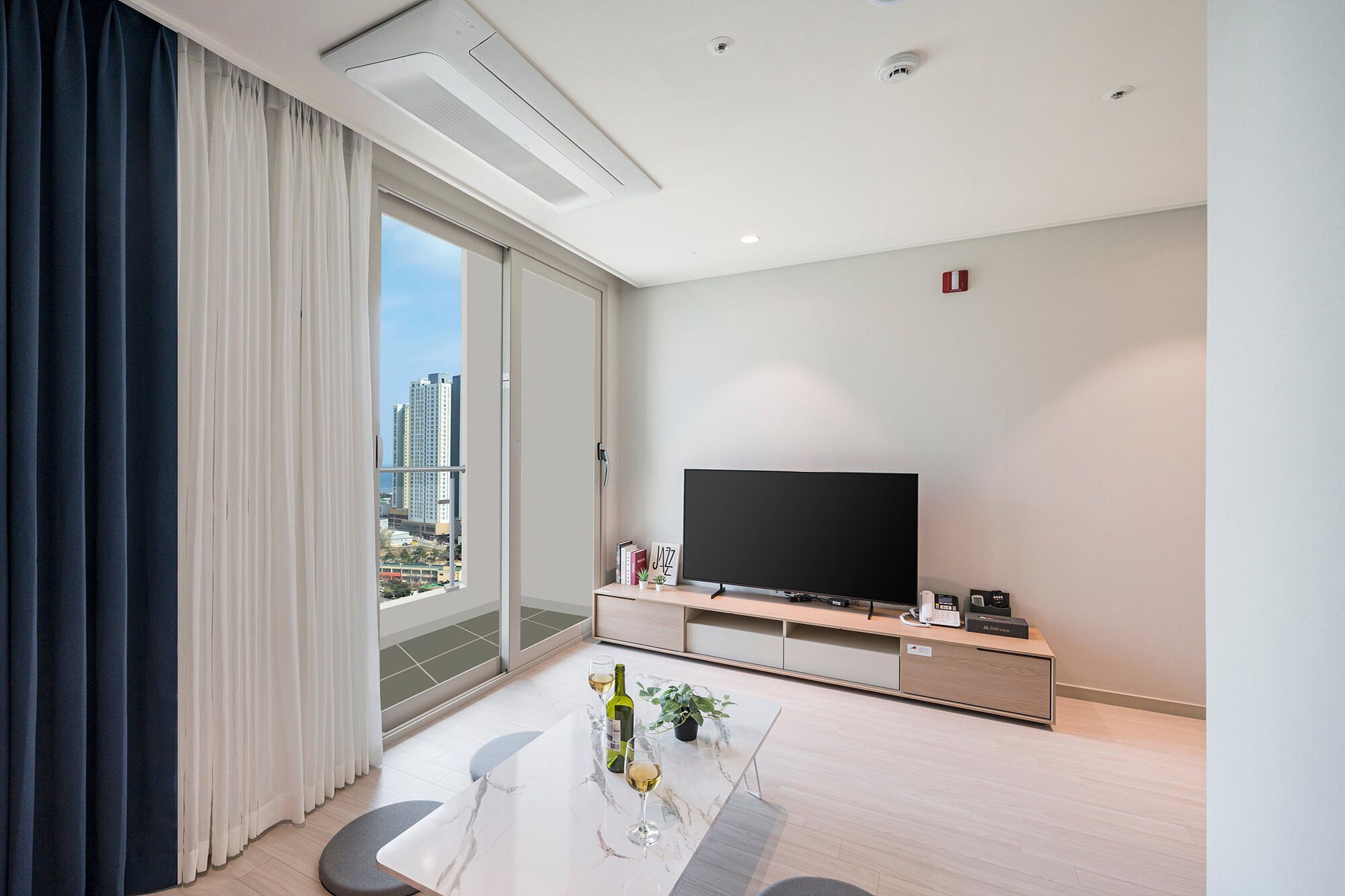 Uma sala de estar moderna com uma grande televisão de tela plana, uma mesa de jantar com cadeiras, uma cafeteira e um vaso de planta.