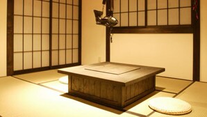 Um espaço com tatames, uma plataforma de madeira, um candeeiro pendurado e um separador shoji.