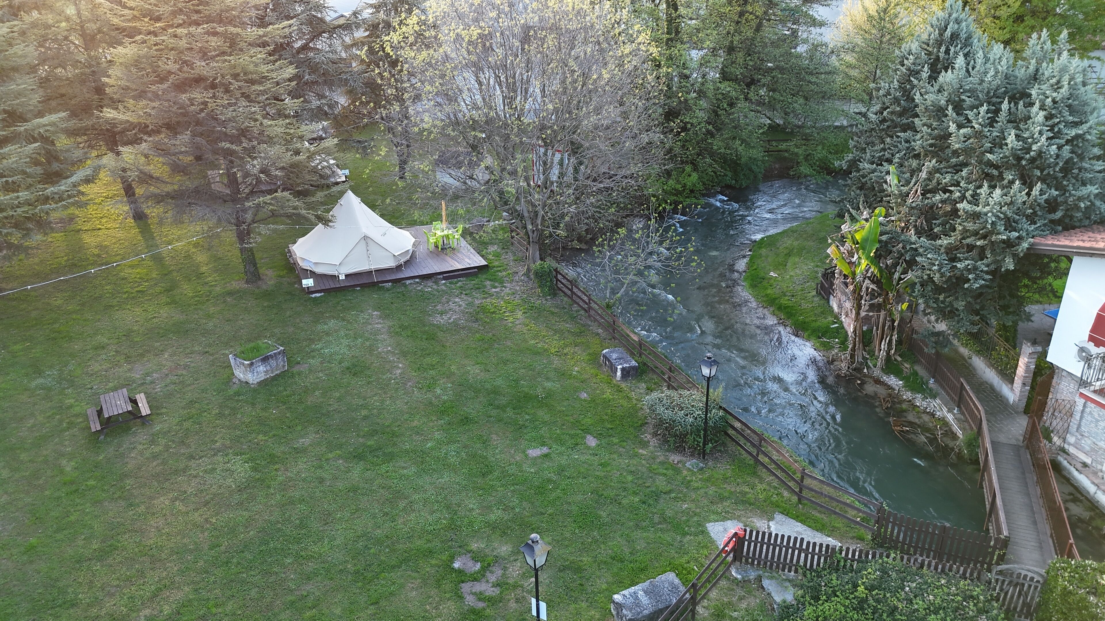 Uma área gramada com uma tenda, um rio pequeno e uma ponte.