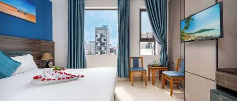Quarto de hotel moderno com cama, escrivaninha, poltrona, televisão e vista para a cidade.