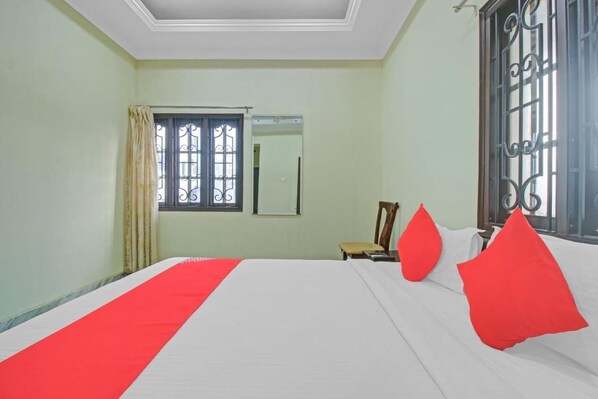 Quarto de hotel com uma cama grande, uma janela com grades de metal, uma cadeira e um espelho na parede.