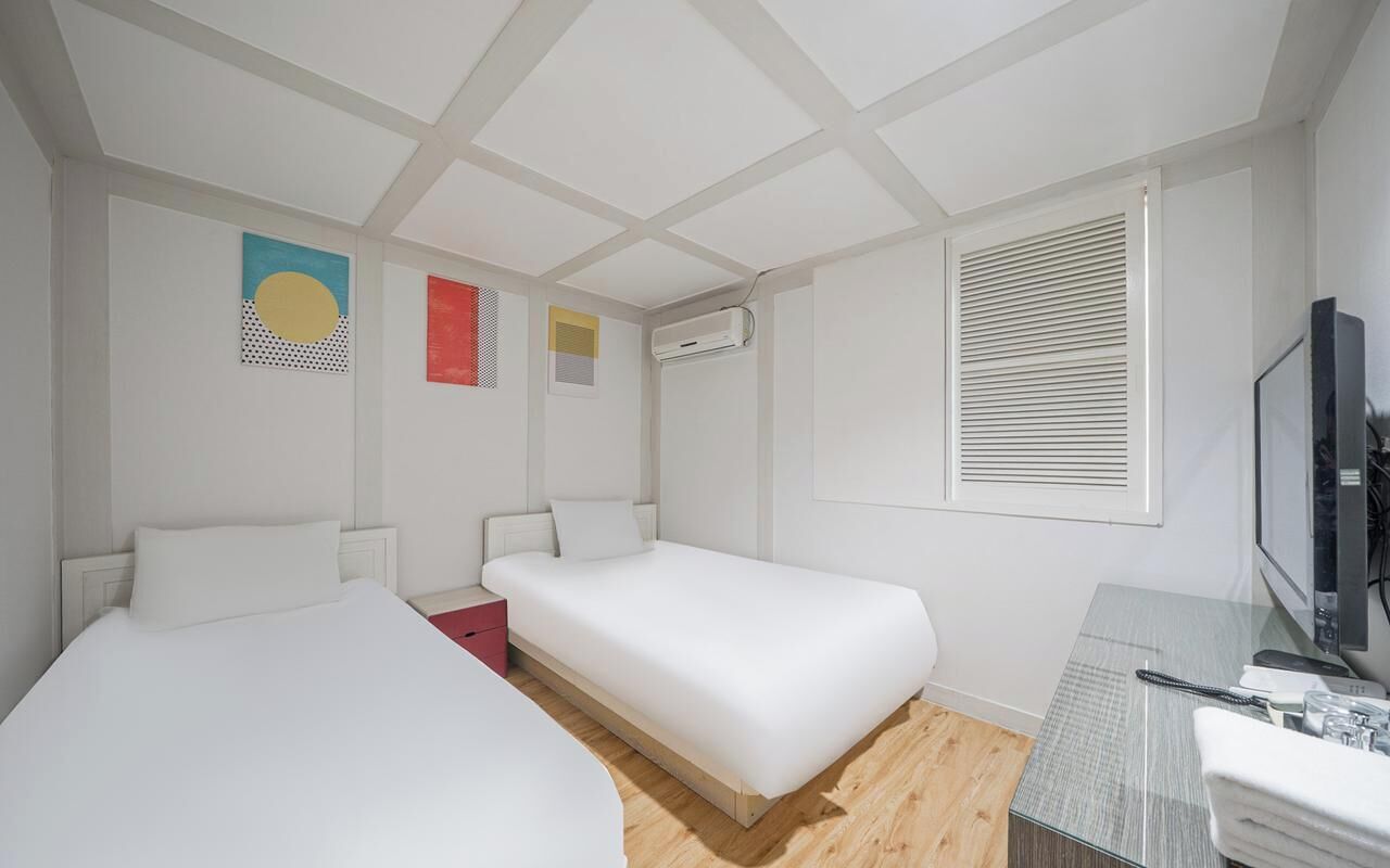Quarto de hotel com duas camas, uma escrivaninha e uma televisão.