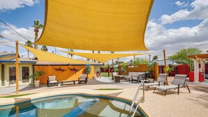 Uma área de piscina com cadeiras de sol e um alpendre coberto com toldo amarelo.
