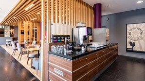 Uma área de bar moderna com teto de ripas de madeira, uma máquina de café e um balcão com copos.