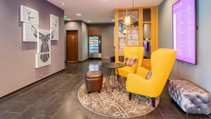 Um lobby moderno com uma mesa de recepção, um painel de chegada digital e uma área de estar com um tapete redondo.