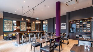 Um restaurante moderno com mesas e cadeiras de madeira, um espaço de bar e uma estante de livros.