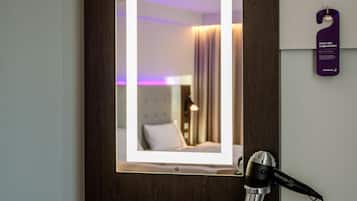 Quarto de hotel com espelho, secador de cabelo, telefone e painel de controle.