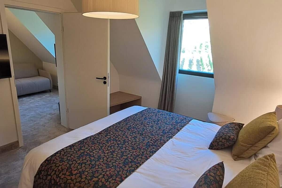 Quarto de hotel moderno com uma cama grande, uma escrivaninha e uma escada para um andar superior.