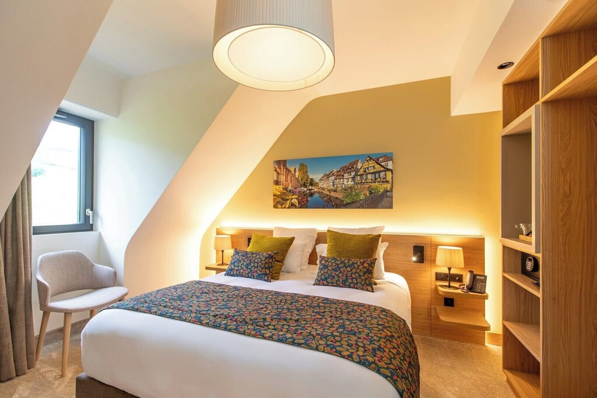 Quarto de hotel moderno com uma cama grande, uma cadeira, uma escrivaninha e um quadro na parede.