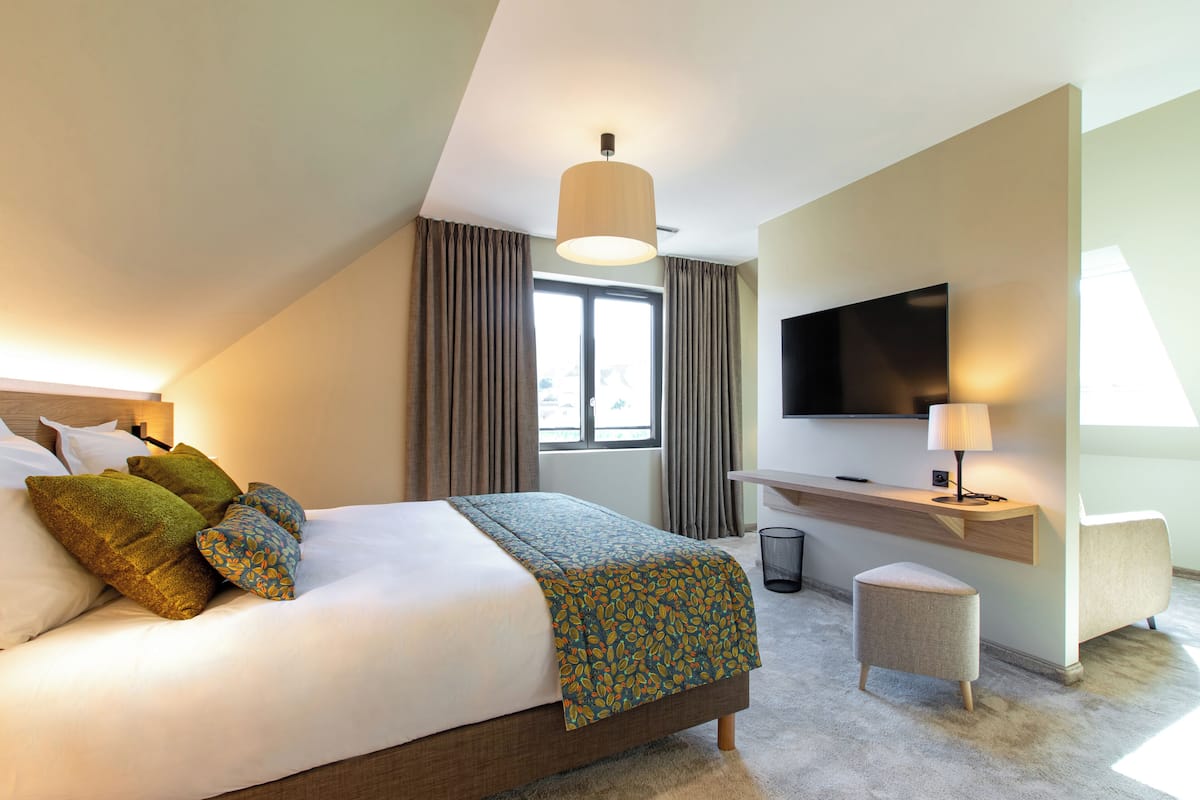 Quarto de hotel moderno com uma cama grande, televisão de tela plana, escrivaninha e janela com cortinas.
