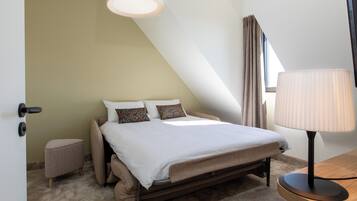 Quarto com cama, mesa de cabeceira, abajur e um banquinho.