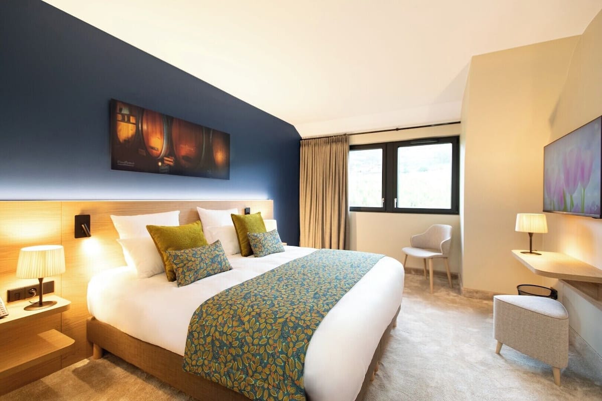 Quarto de hotel com uma cama grande, uma escrivaninha, uma cadeira e uma janela.