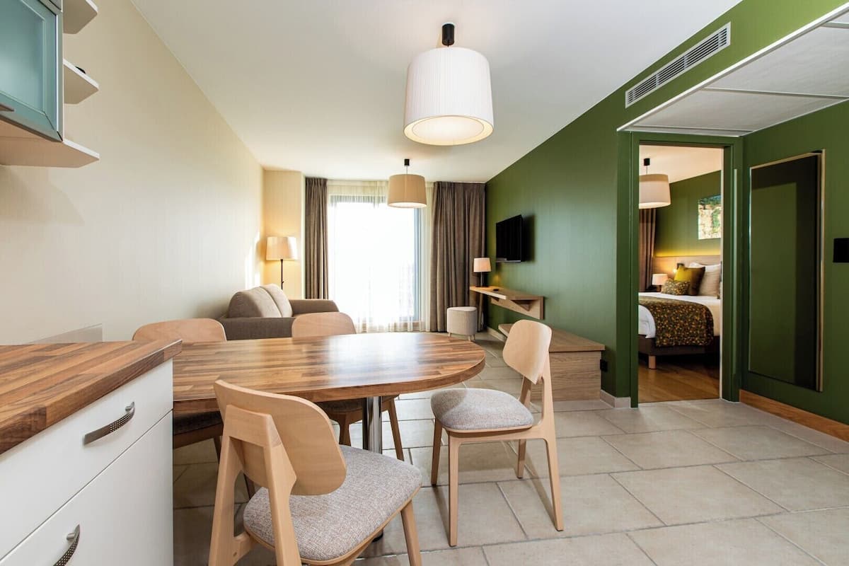 Quarto de hotel com área de refeições, cama, televisão e uma parede de destaque verde.