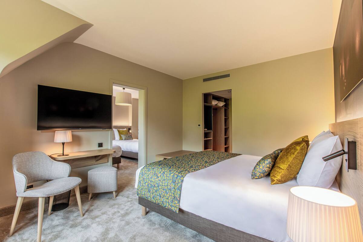 Quarto de hotel com cama, escrivaninha, cadeira, televisão e armário.