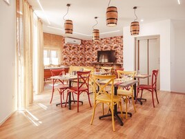 Uma área de jantar com piso de madeira, cadeiras vermelhas e amarelas e uma parede estampada.