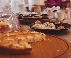 Diversos doces em uma mesa, incluindo um pastel coberto, um prato com cupcakes e uma tigela com sobremesa coberta de raspas de chocolate.