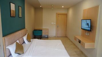 Quarto de hotel com cama, secretária, cadeira, televisão e porta.