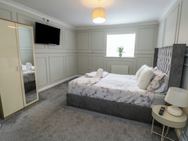 Quarto com cama, televisão, janela, espelho e mesa de cabeceira com abajur.