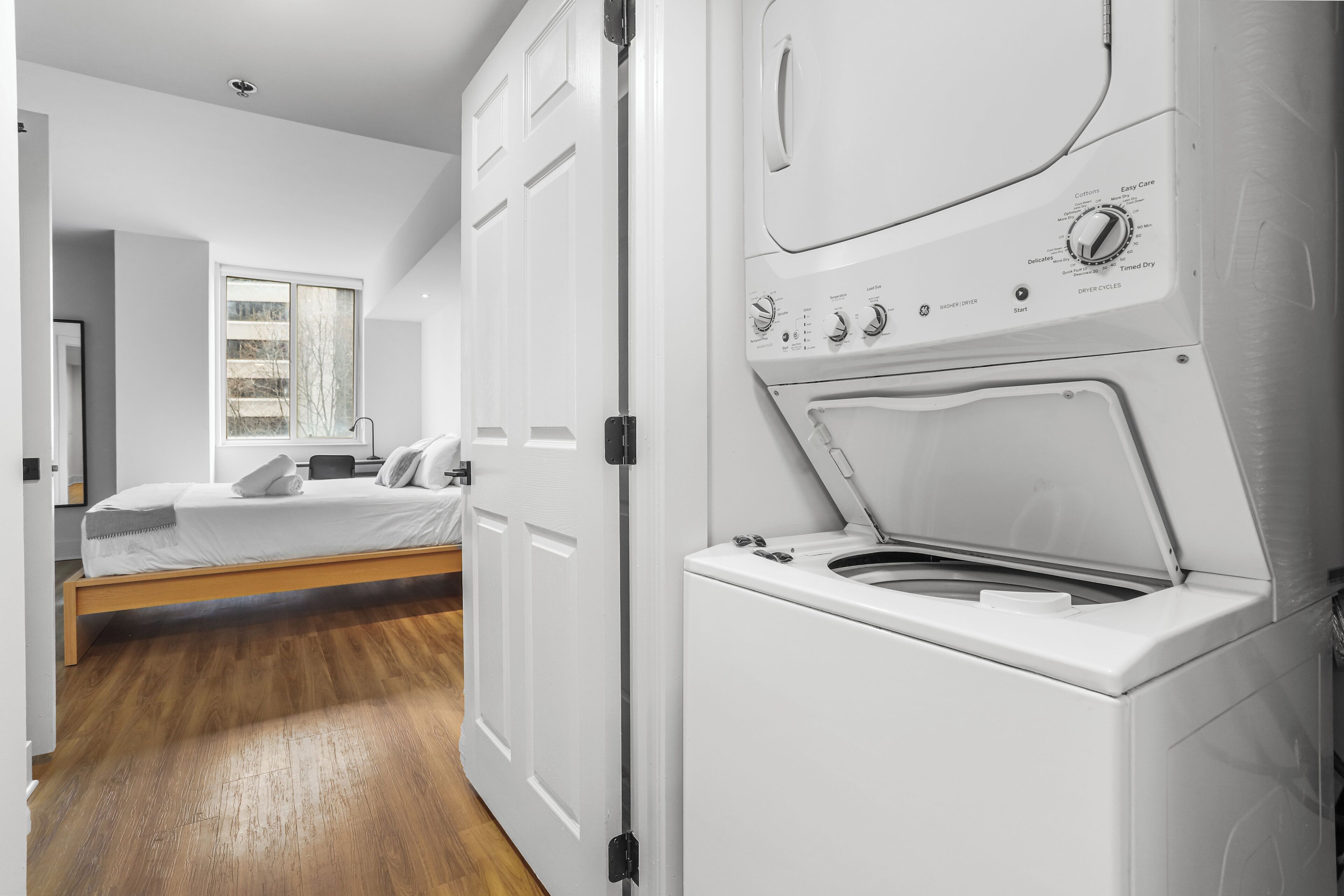 Quarto moderno com cama, máquina de lavar e uma grande janela.