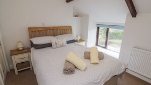 Quarto com cabeceira de madeira, cama grande com roupa de cama estampada, duas mesas de cabeceira com abajures, janela com vista para o verde e um radiador.