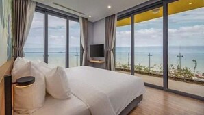 Quarto moderno com cama grande, televisão de tela plana e varanda com vista para o mar.