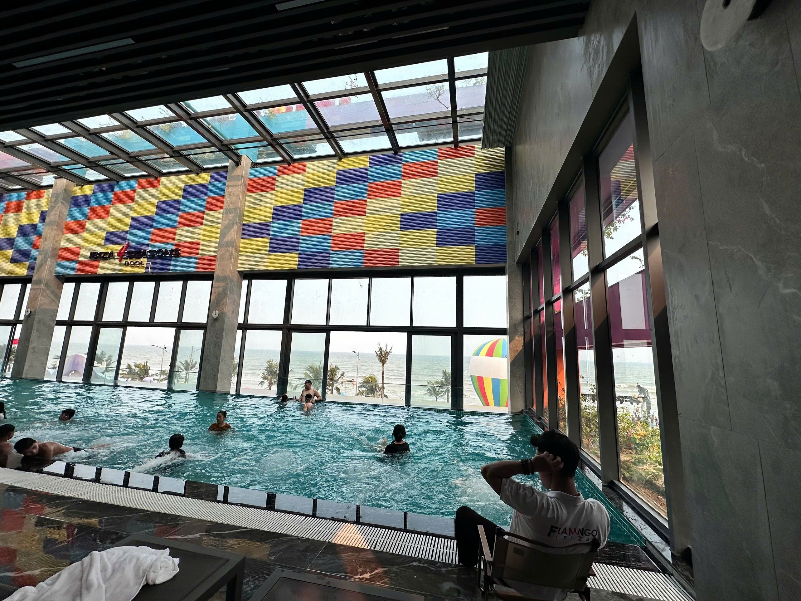 Piscina interna com amplas janelas e parede colorida.
