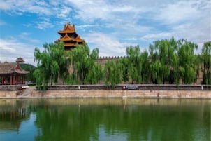 Um edifício tradicional chinês refletido na água, com uma parede de pedra e árvores.