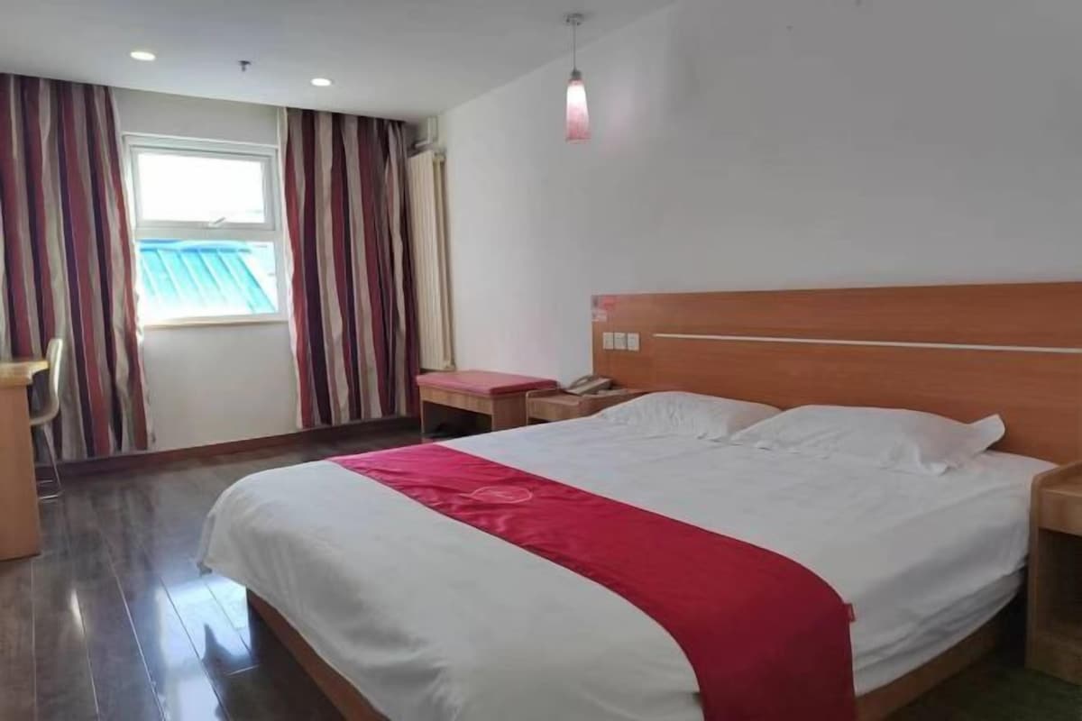 Quarto de hotel com cama, mesa de cabeceira e janela com cortinas.