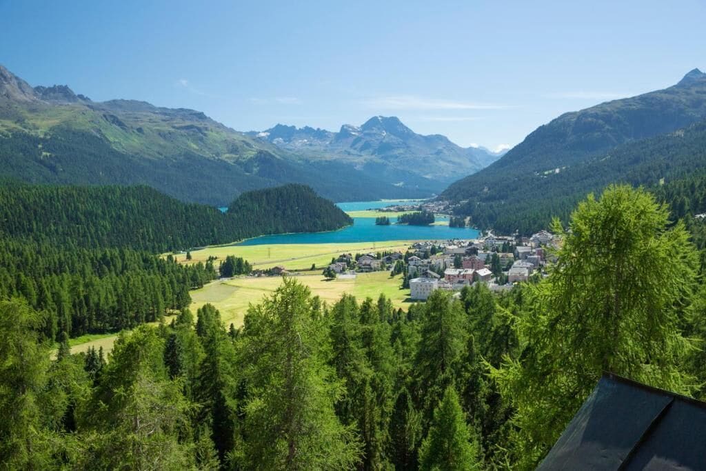 Paisagem montanhosa com um lago, uma cidade e floresta densa.