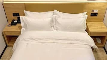 Uma cama bem arrumada com lençóis brancos, um telefone ao lado da cama e uma pequena mesa de cabeceira de madeira.