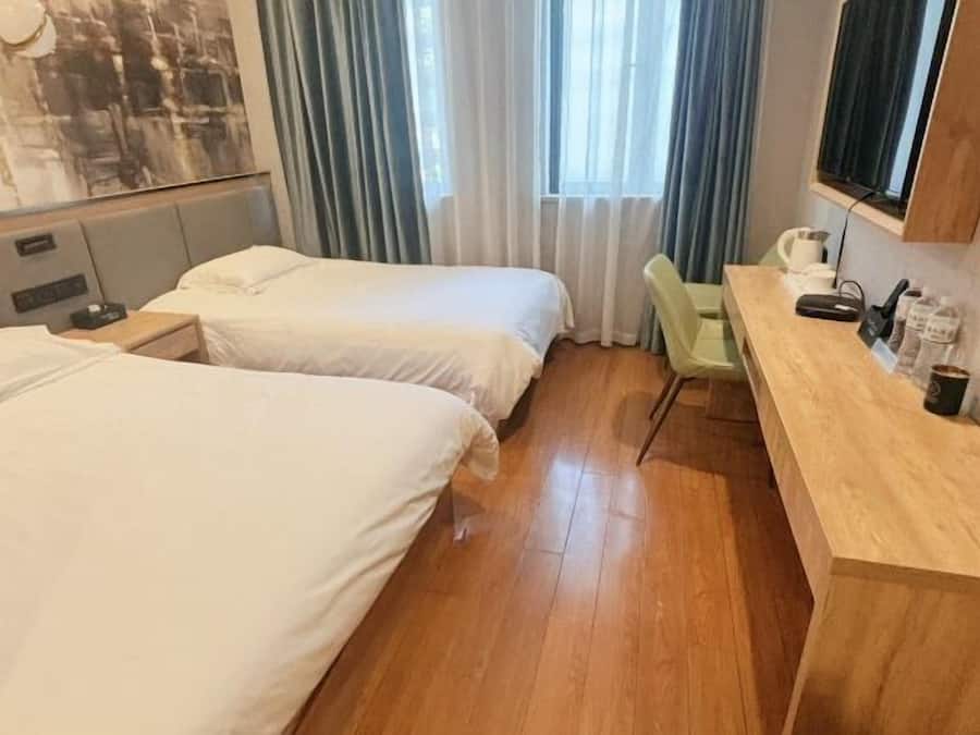 Quarto de hotel com duas camas, uma escrivaninha de madeira, uma cadeira, televisão e uma janela com cortinas.