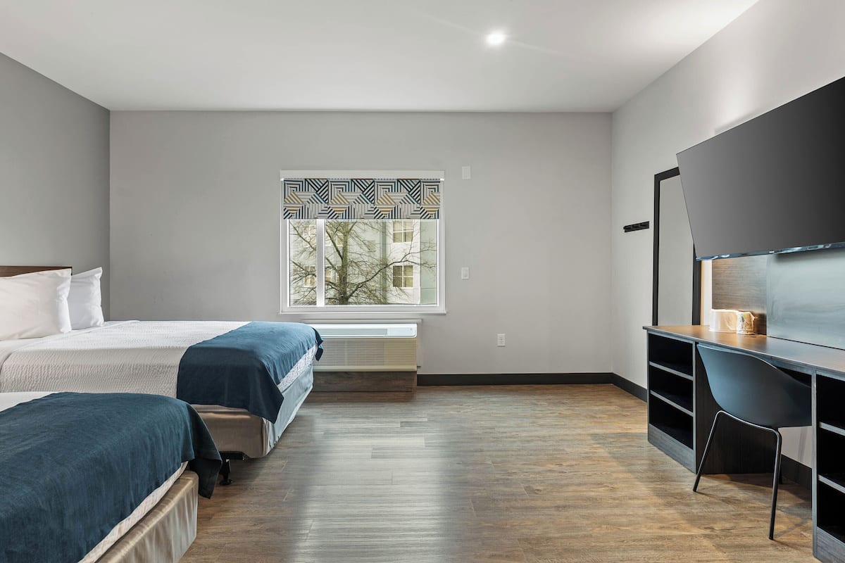 Quarto de hotel moderno com duas camas, uma escrivaninha e uma janela grande.