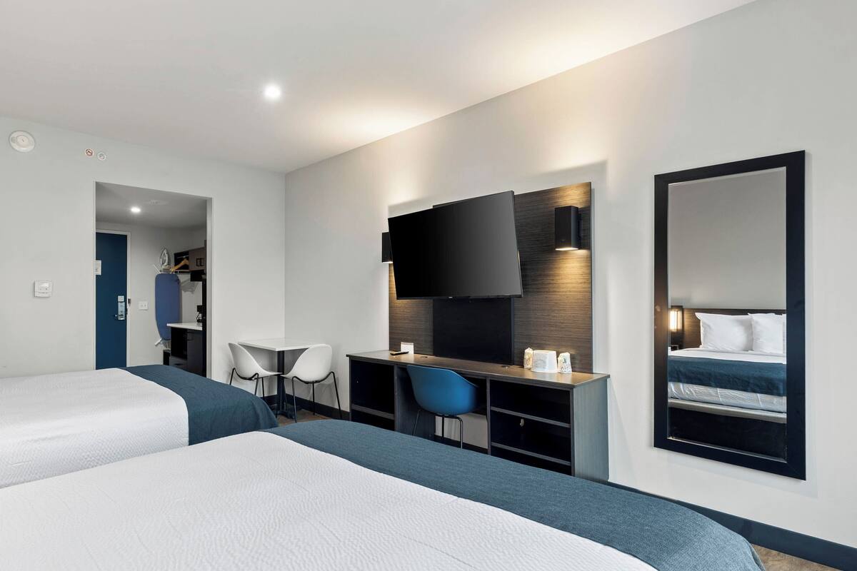 Quarto de hotel com duas camas, uma escrivaninha, uma cadeira, uma TV e um espelho.