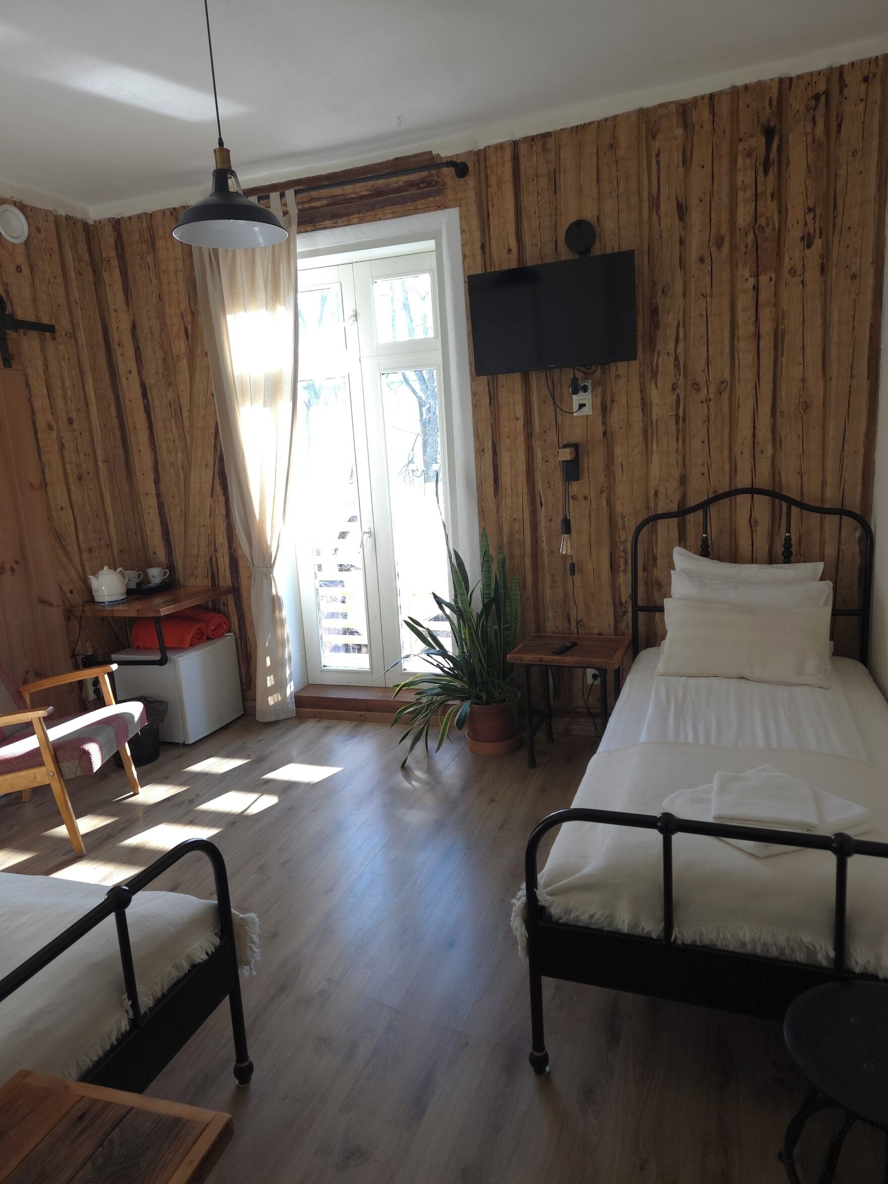 Quarto com paredes de madeira, uma cama, escrivaninha, cadeira, planta em vaso e televisão.