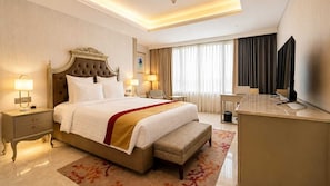 Quarto de hotel com uma cama grande, mesas de cabeceira, escrivaninha, cadeira, televisão e uma janela ampla com cortinas.
