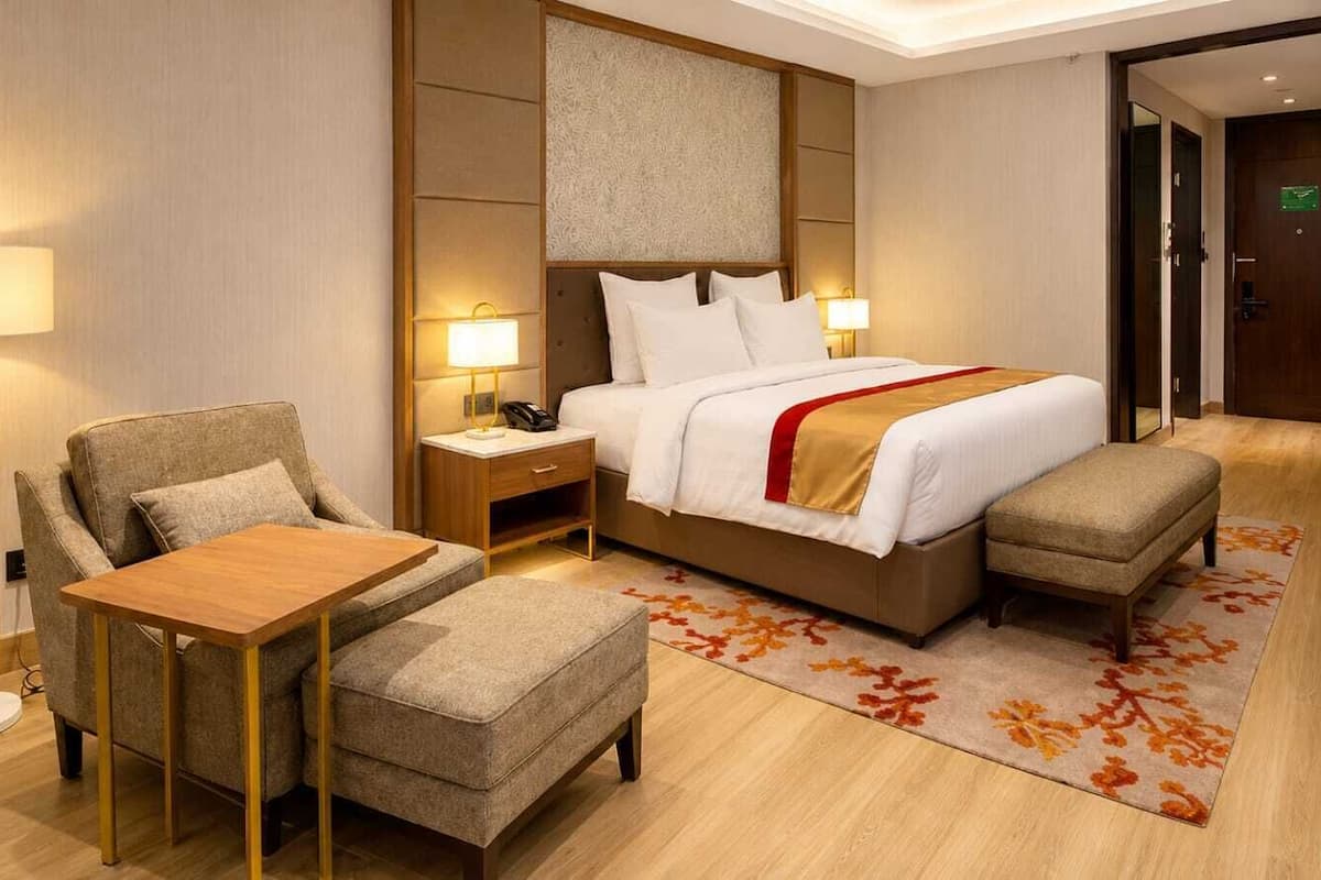 Quarto de hotel com cama, mesas de cabeceira, escrivaninha, cadeira e abajur.