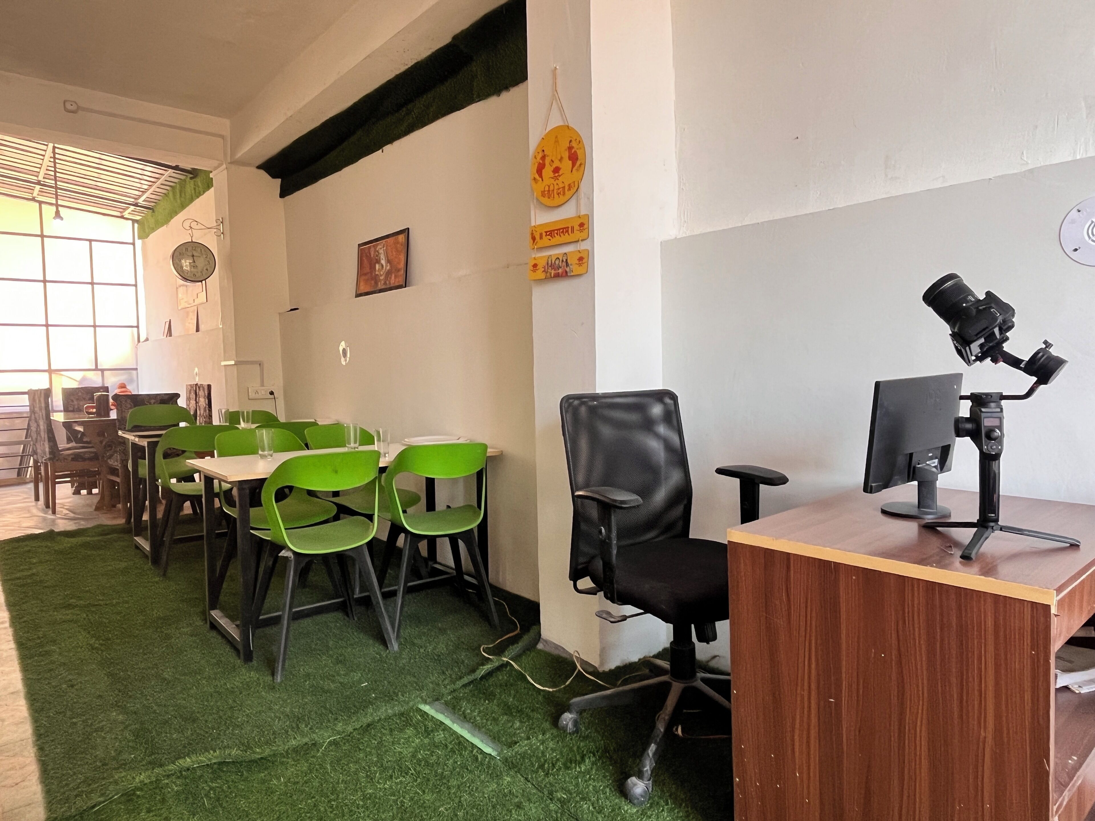 Quarto com cadeiras verdes, uma escrivaninha de madeira e um equipamento de filmagem.