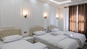 Quarto de hotel com três camas, um candelabro e uma janela grande com cortinas.