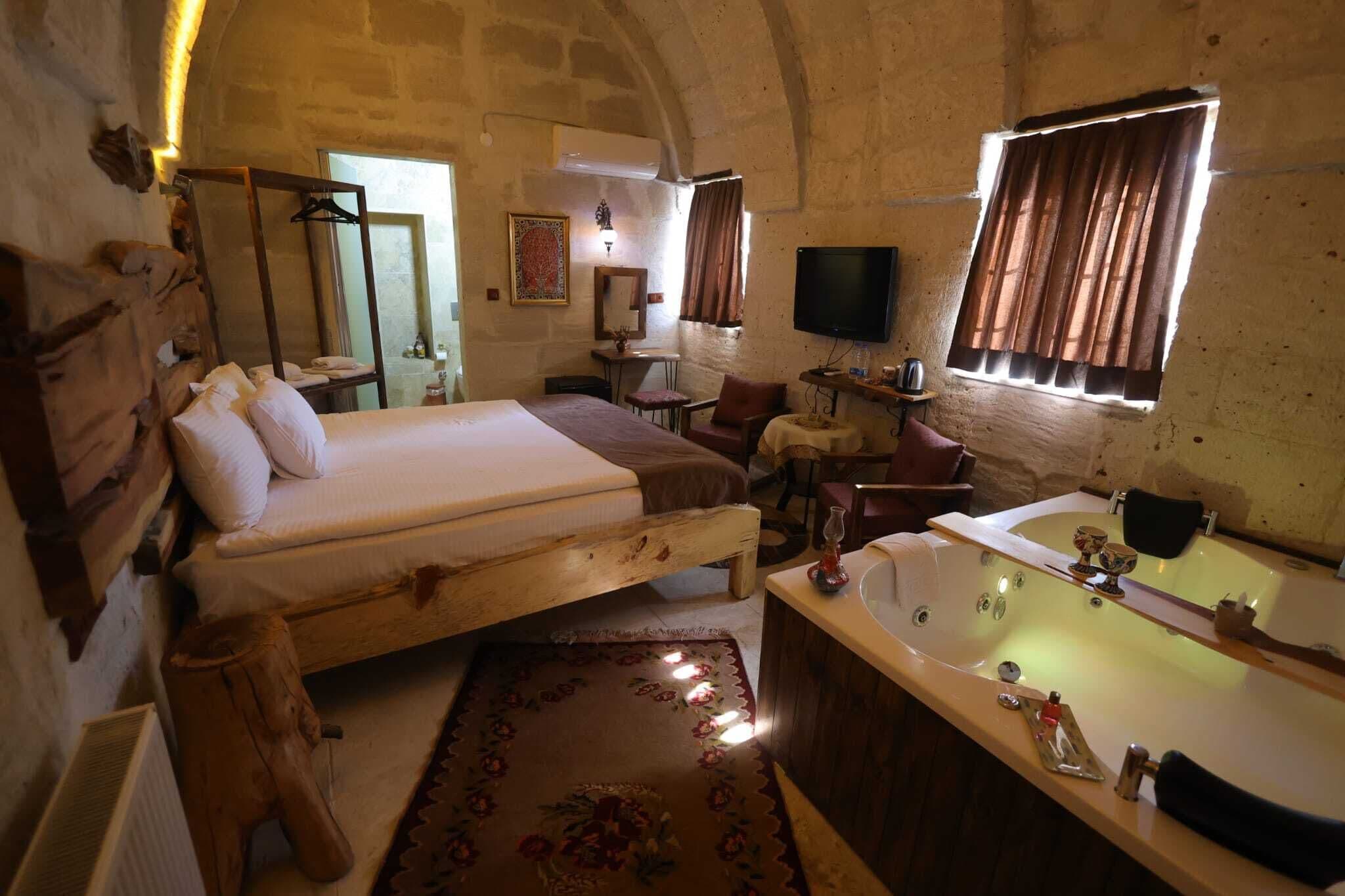 Quarto rústico com cama de madeira, uma banheira grande, televisão e uma pequena mesa com uma cadeira.