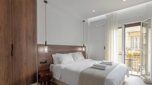 Quarto moderno com guarda-roupa de madeira, uma cama grande com roupa de cama branca e uma varanda com vista.