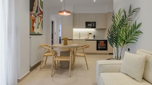 Uma sala de estar moderna com uma mesa de jantar redonda e cadeiras, um sofá, uma grande planta em vaso e uma área de cozinha com micro-ondas e forno.