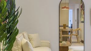 Uma sala de estar moderna com um sofá, uma mesa de centro e um espelho refletindo uma área de jantar com mesa e cadeiras.